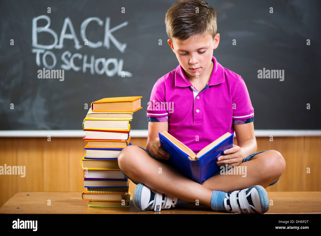 Cute school boy reading book in classroom against blackboard Stock ...