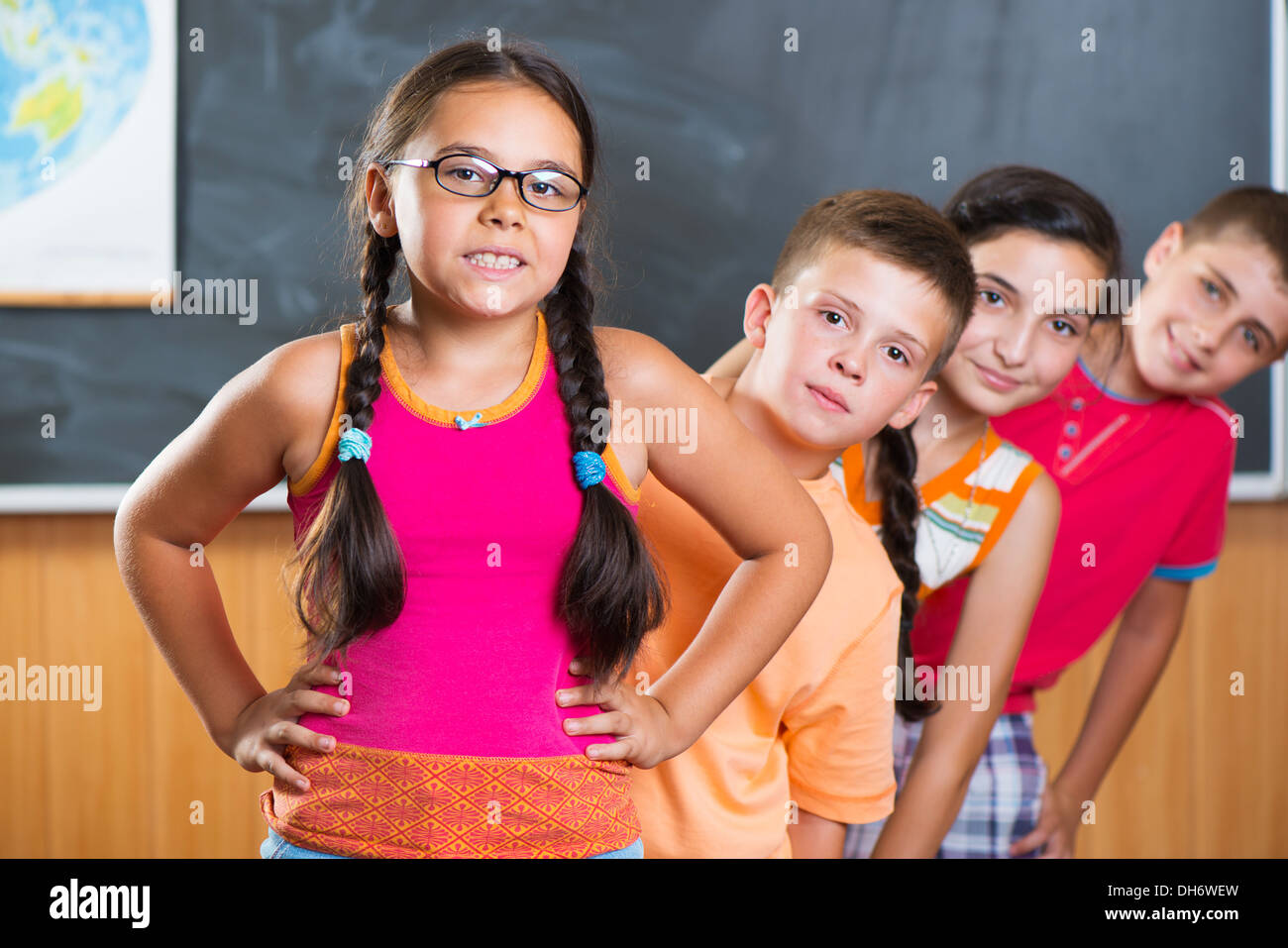 Four smiling schoolchildren standing in classroom against blackboard ...