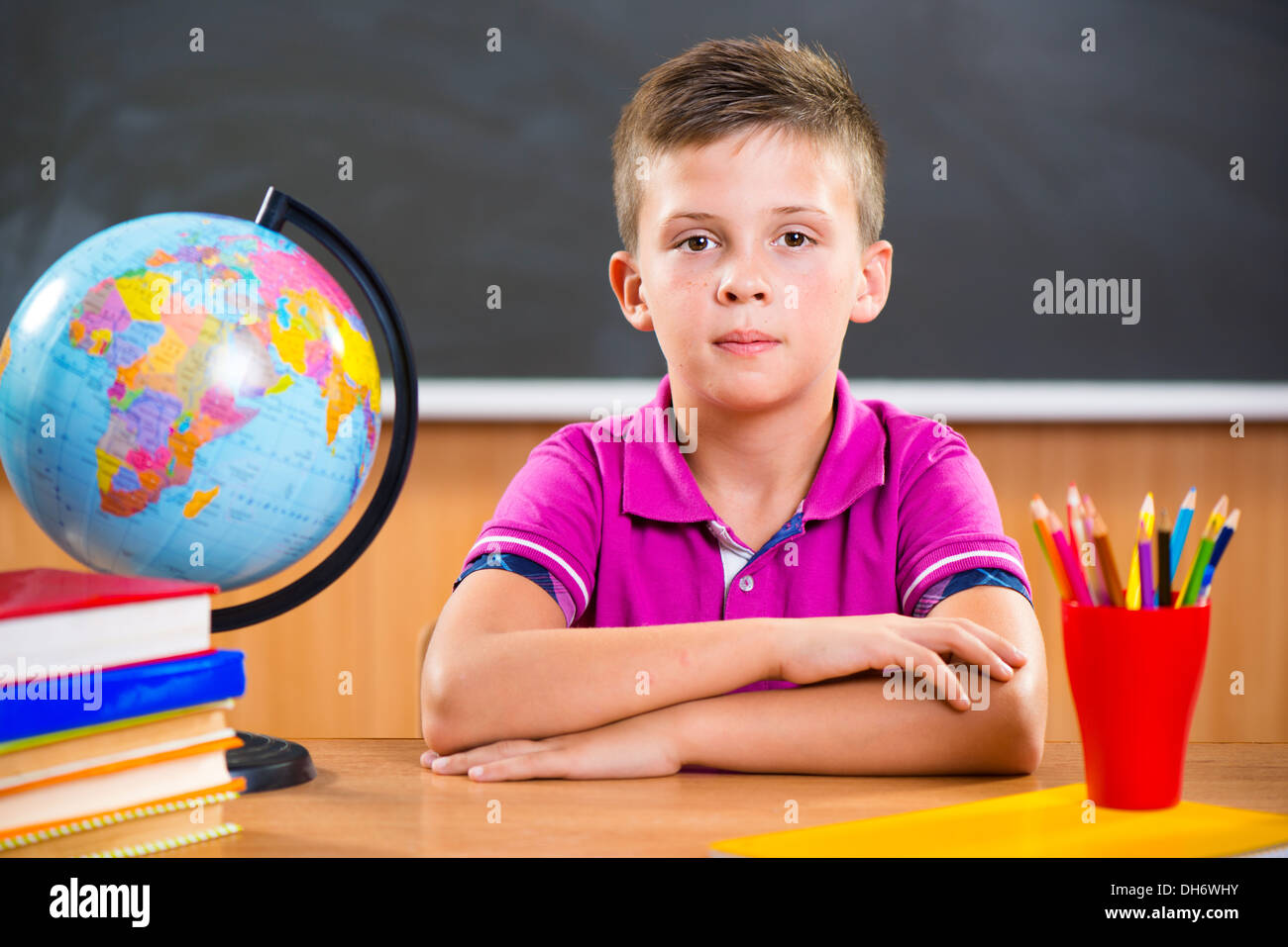 Cute diligent boy sitting in classroom in front of blackboard Stock ...