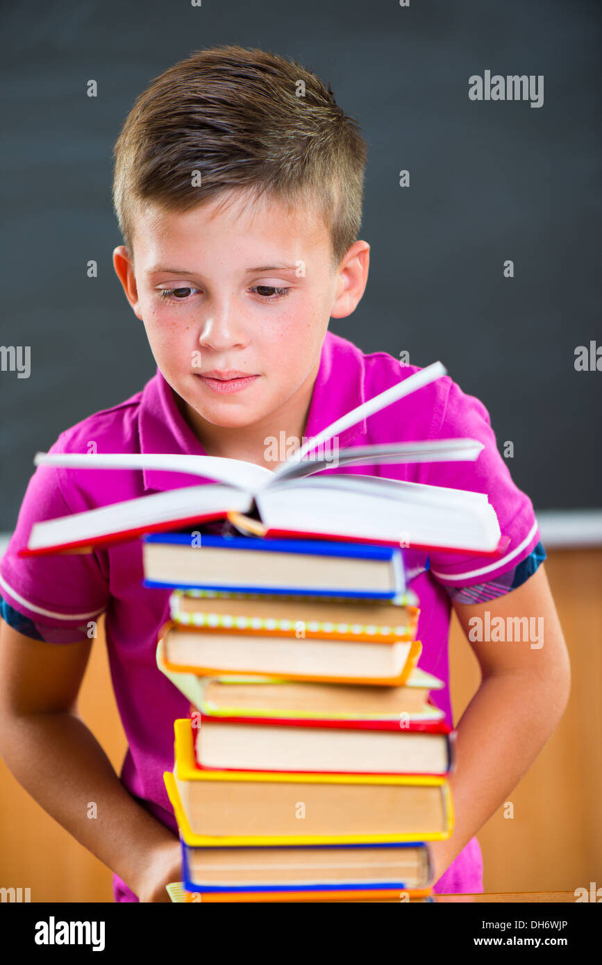 Adorable schoolboy with stack of books in classroom Stock Photo - Alamy