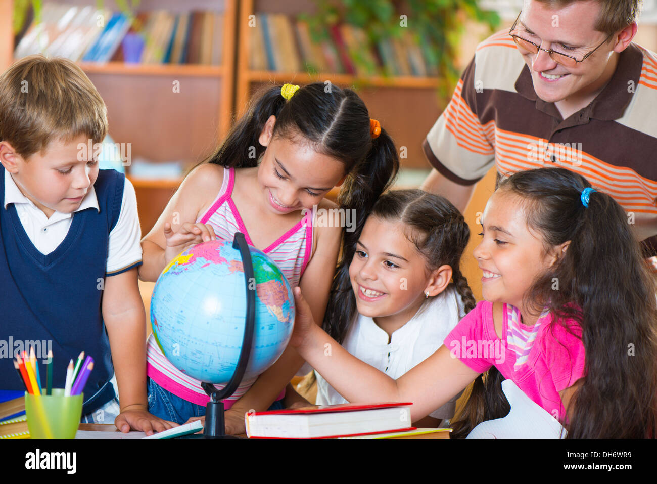 Portrait of pupils looking at globe with their teacher during geography ...