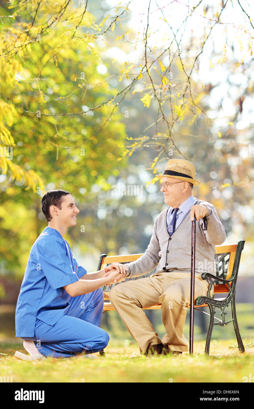 Male healthcare professional helping senior man sitting on a bench in a ...
