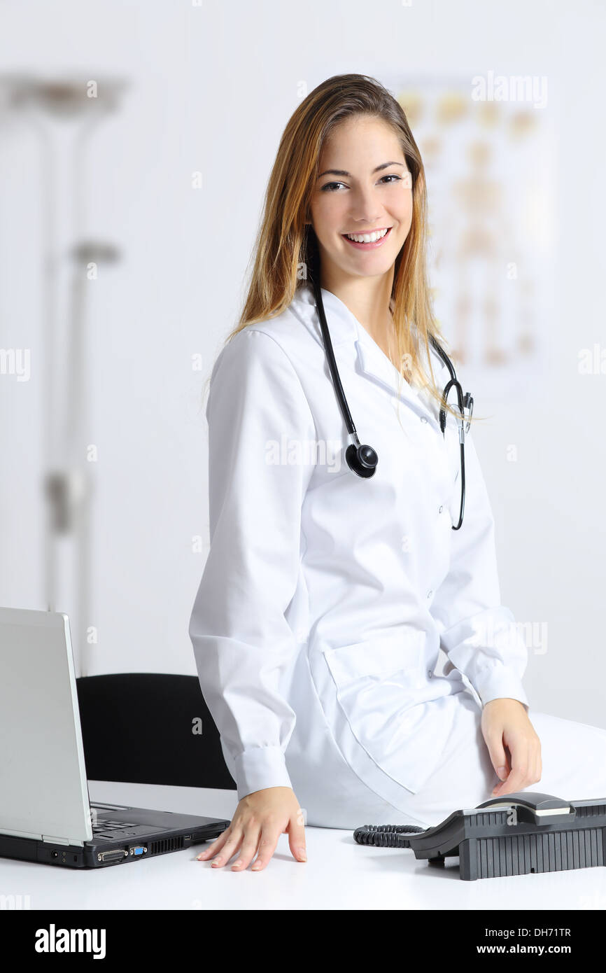 Beautiful female doctor sitting on the desk of her consultation Stock ...