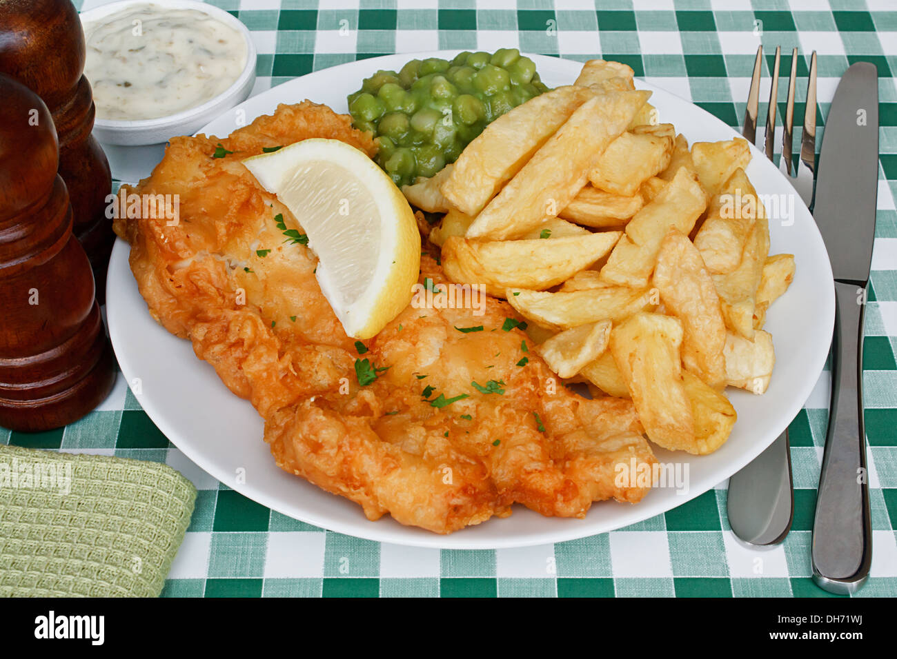 Plate of fish and chips with mushy peas and a slice of lemon on a diner table. A traditional ...