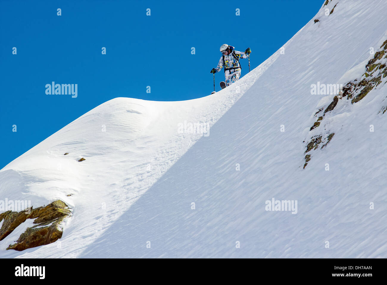 Skier in front of the steep, snow-covered slope against the clear, blue ...