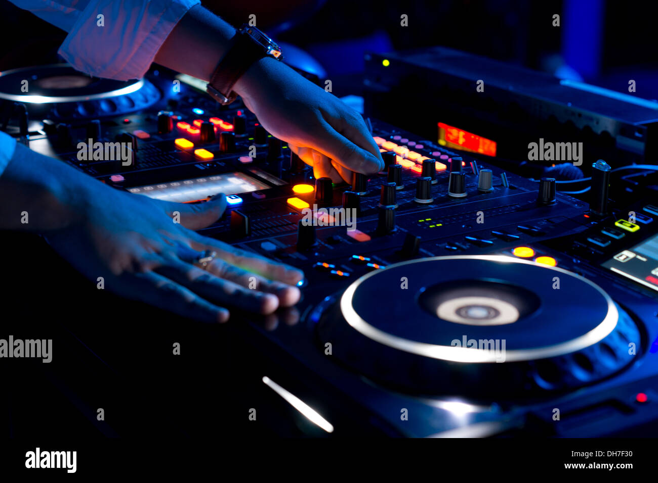 Hands of a DJ mixing music at a disco or concert with one hand on the ...
