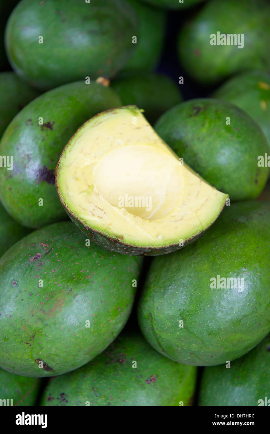 Pile of fresh green avocados with cut sample on display at farmers ...