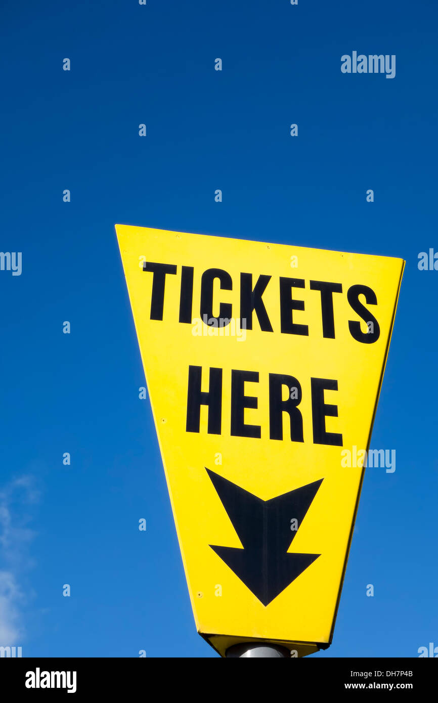 A yellow 'tickets here' sign with an arrow pointing downwards, against ...