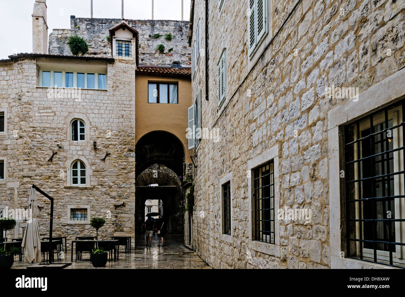 People walk along an ancient marble pathway through an arched gate ...