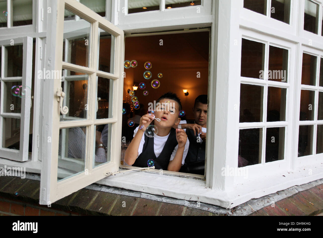 Children blows bubbles out of a window of pub at a wedding, Sussex, UK ...