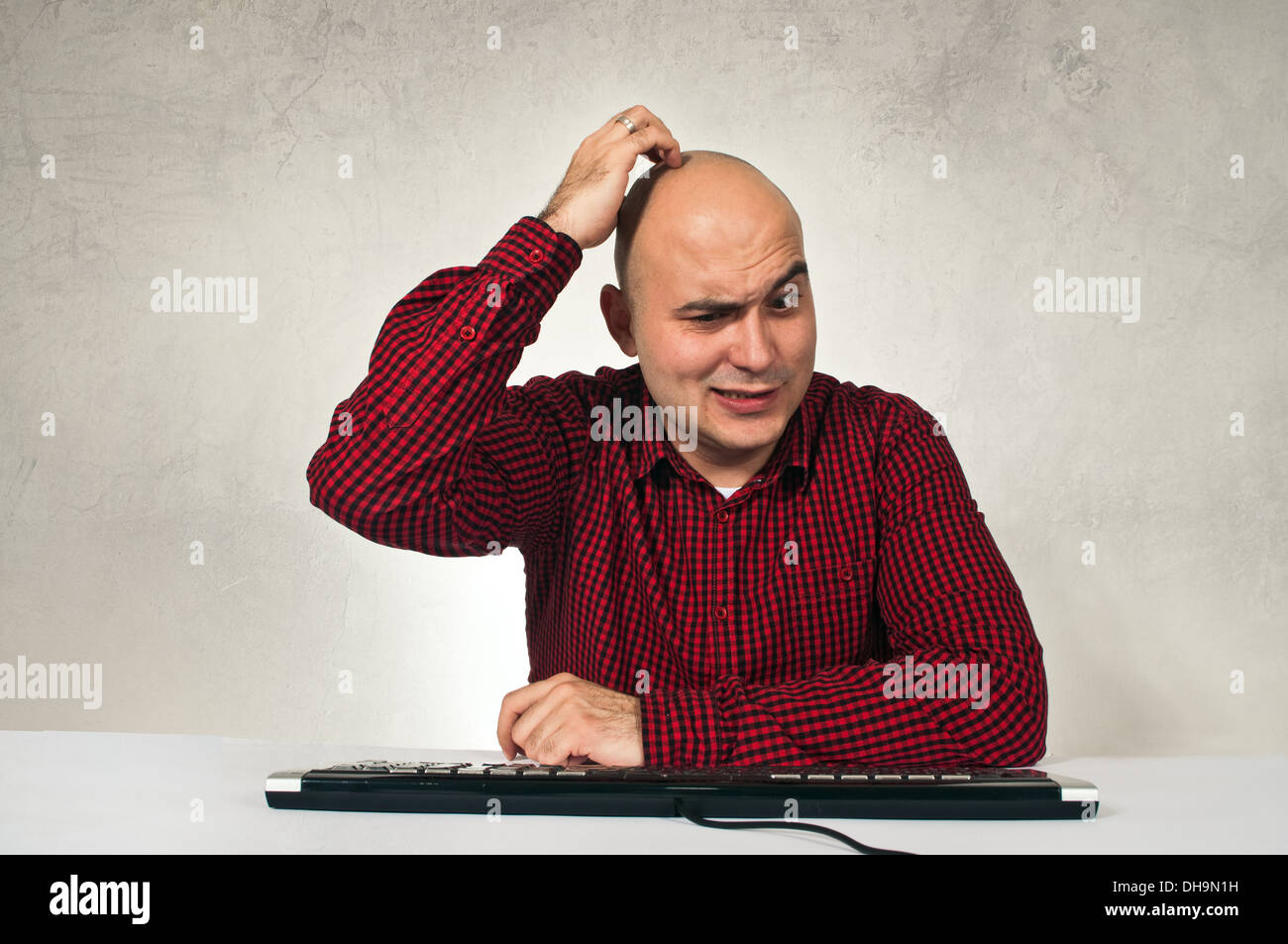 Confused man sitting at office table in front of the computer keyboard ...