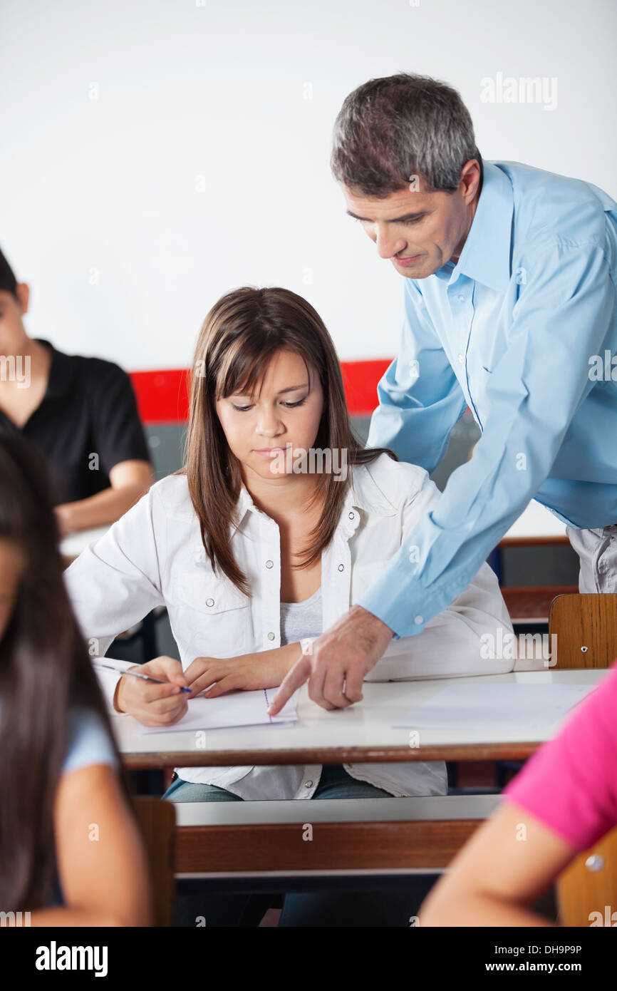 Male Teacher Assisting Female Student At Desk Stock Photo - Alamy