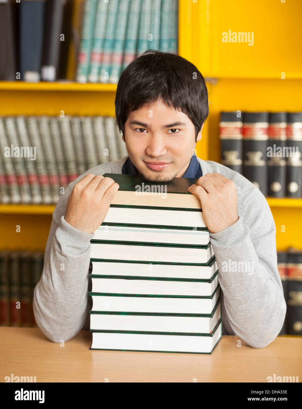 Confident Man With Stacked Books Sitting In University Library Stock ...
