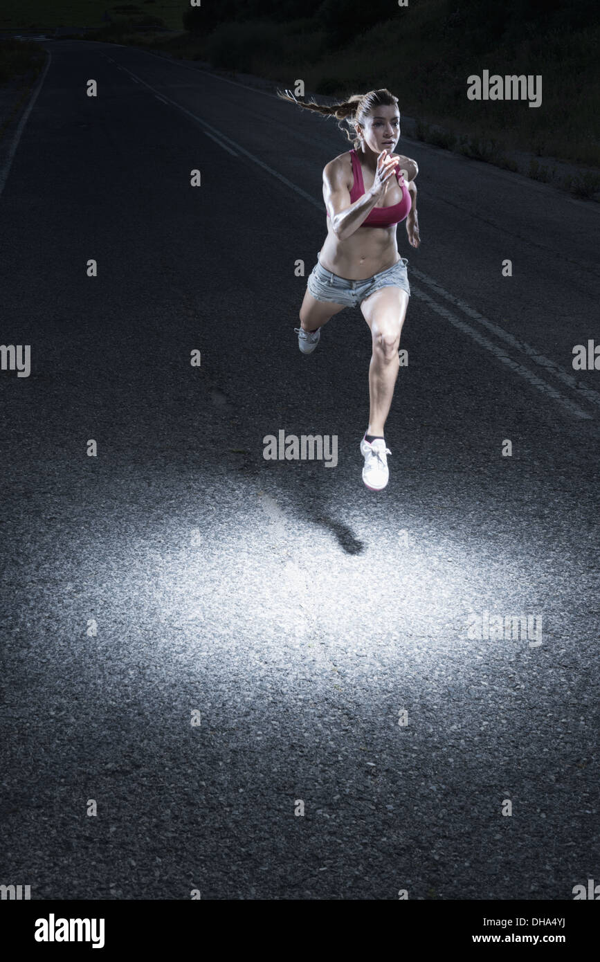 A Woman Running Down A Paved Road At Night With A Spotlight ...