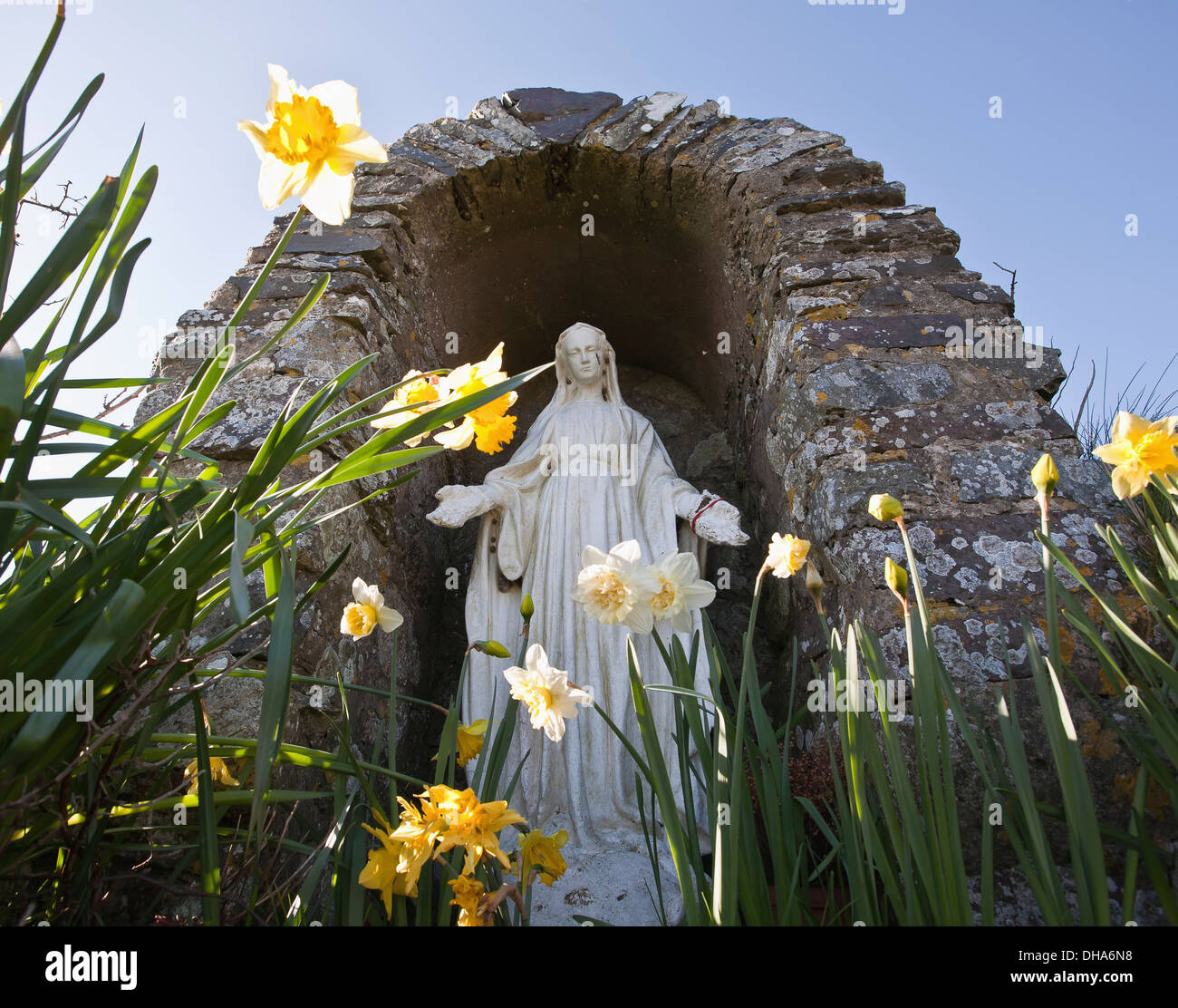 A Religious Statue Inside An Arch Stone Structure And Daffodils Growing ...
