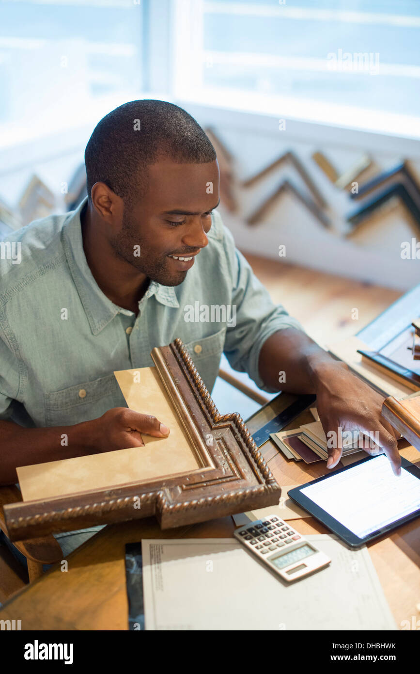 A young man at his workbench in a picture framing studio. Surrounded by ...
