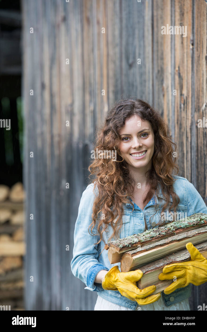 A woman carrying an armful of firewood from the logstore on the farm ...