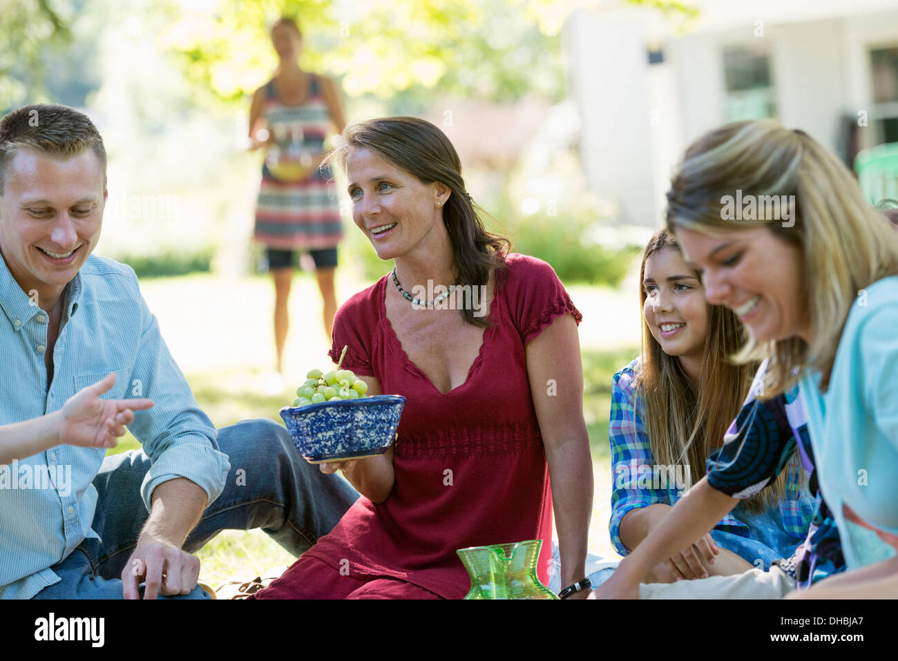 A group of adults and children sitting on the grass under the shade of ...