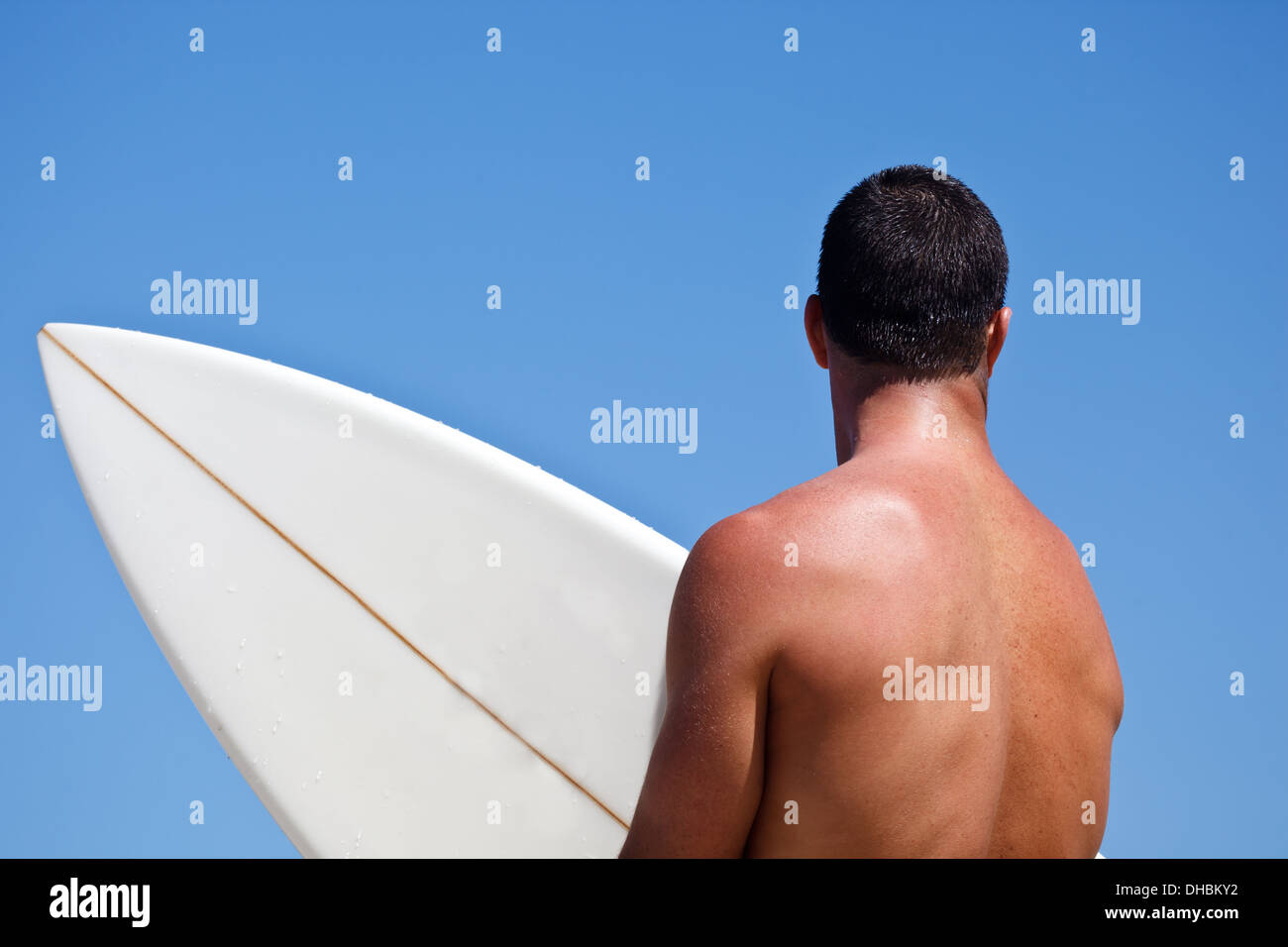 Man holding his surfboard up in front of him, back turned to camera ...