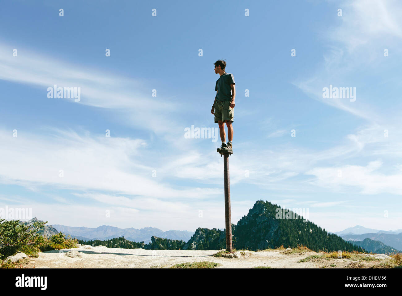 A man standing balancing on metal post looking towards expansive sky on ...