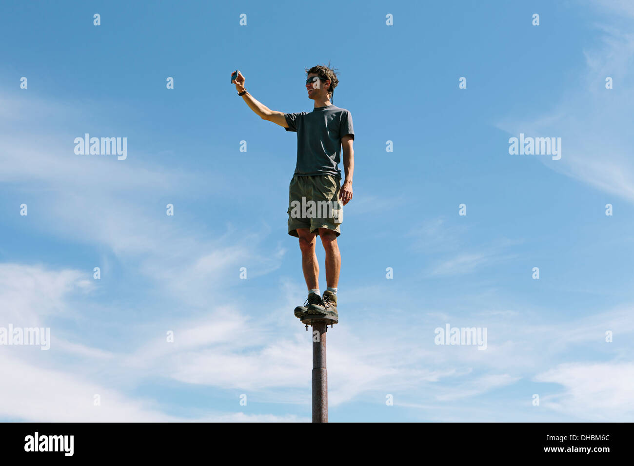 Man standing balancing on metal post looking towards expansive sky on ...