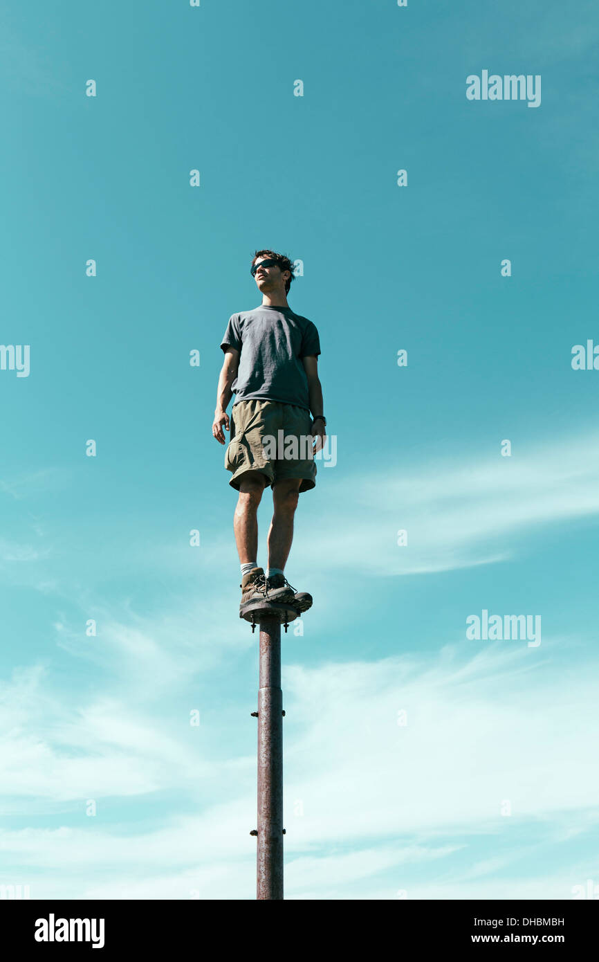 Man standing balancing on metal post looking towards expansive sky ...