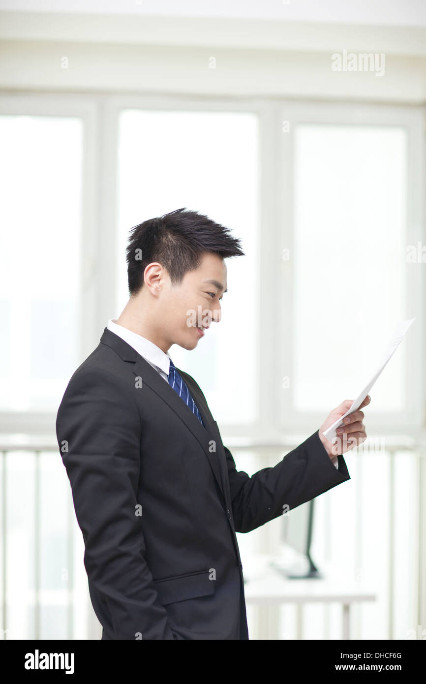 Portrait of young businessman standing,looking documents and holding ...