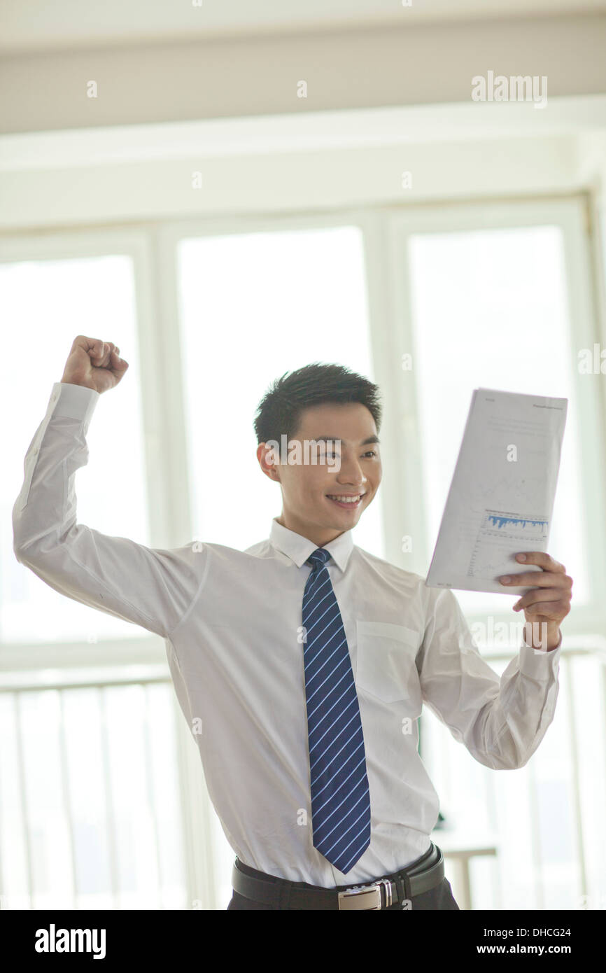 Portrait of young businessman standing,looking documents and holding ...