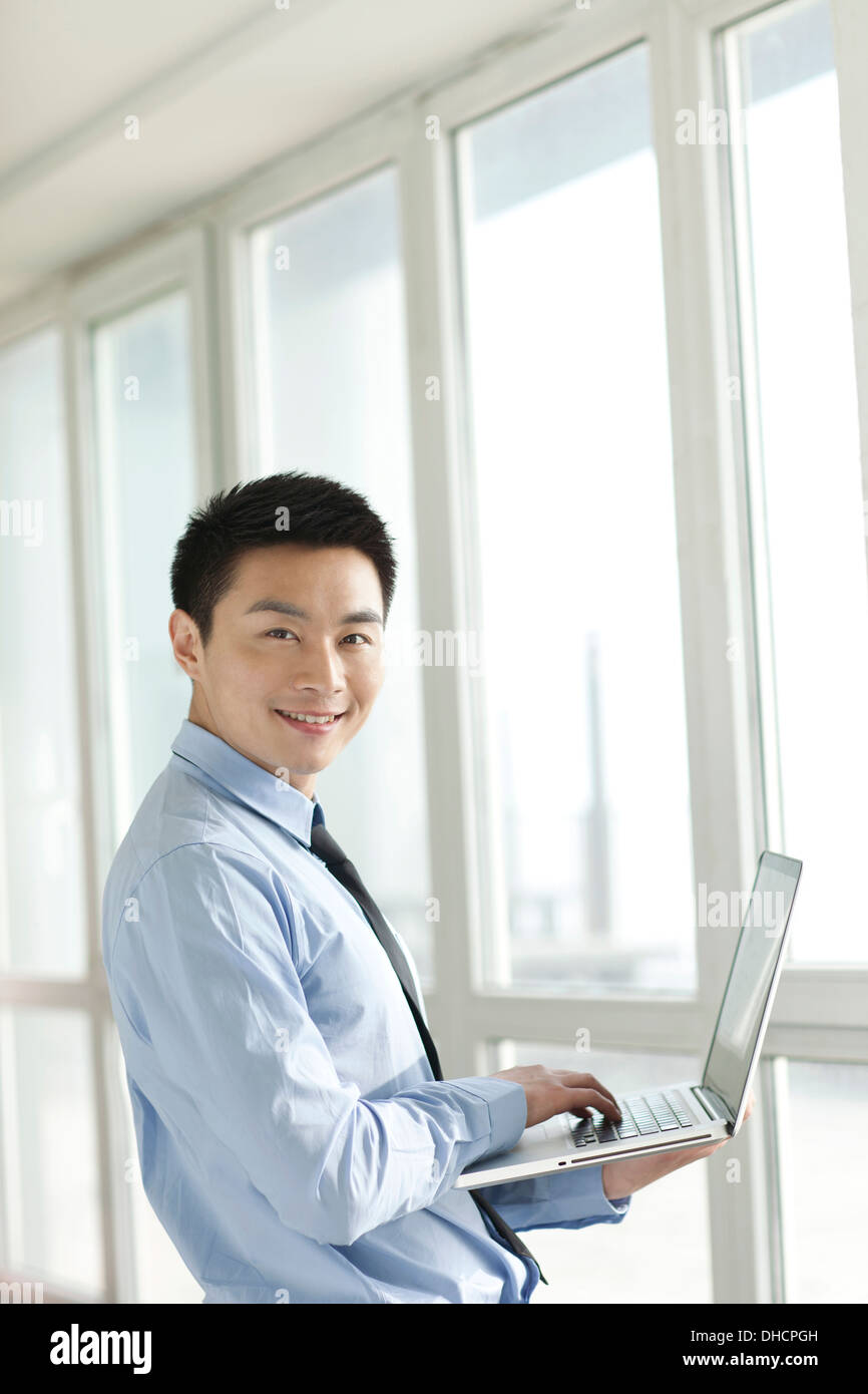 Portrait of young businessman holding laptop in corridor Stock Photo ...