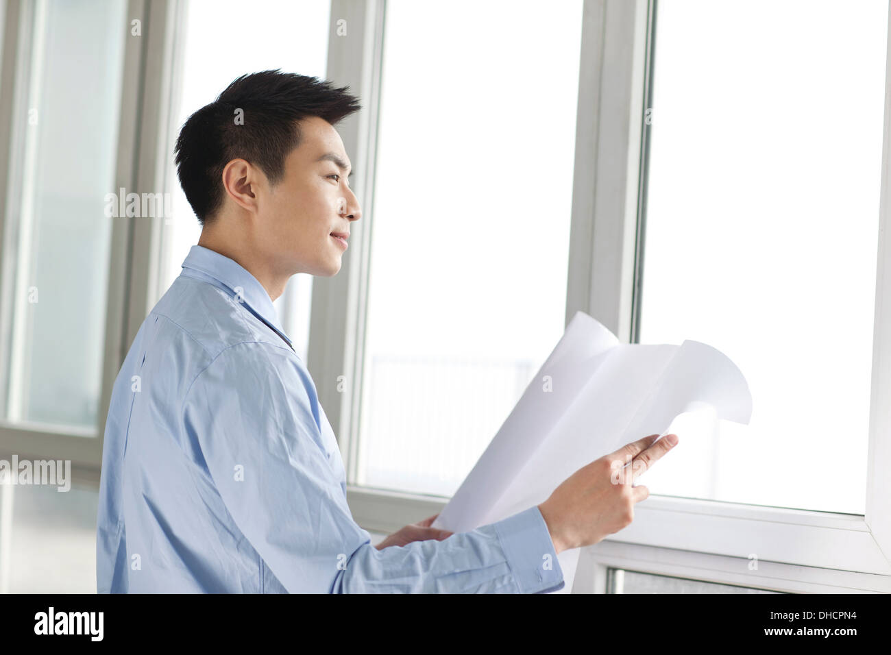 Portrait of young businessman holding blueprint in corridor Stock Photo ...