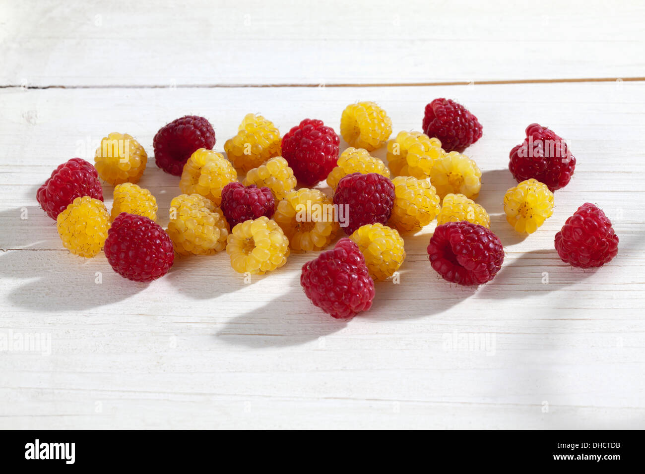 Yellow and red raspberries (Rubus idaeus) on white wooden table, studio ...