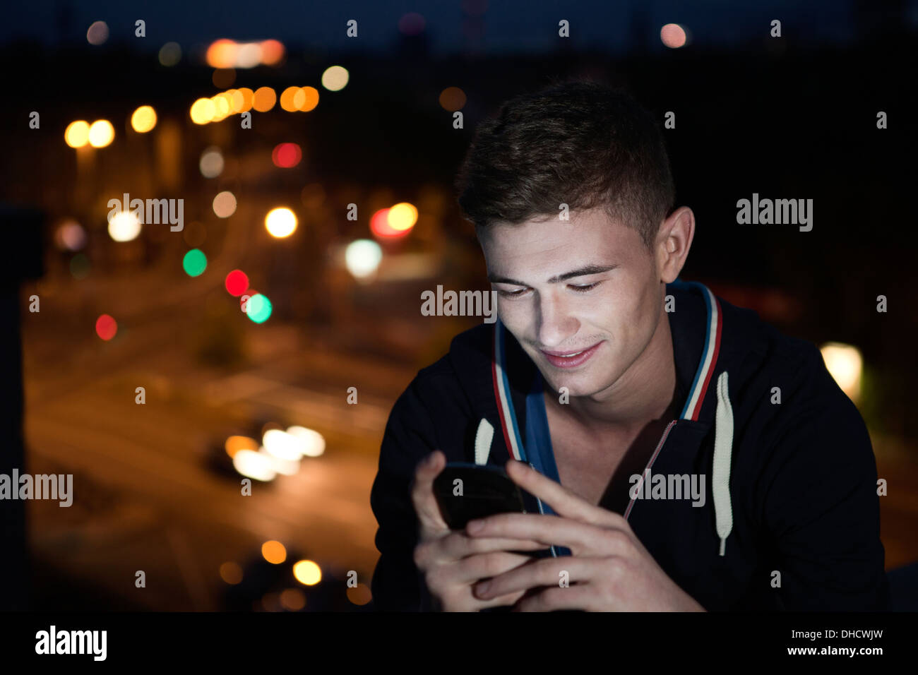 Young man with smartphone sitting on flat roof by night Stock Photo - Alamy