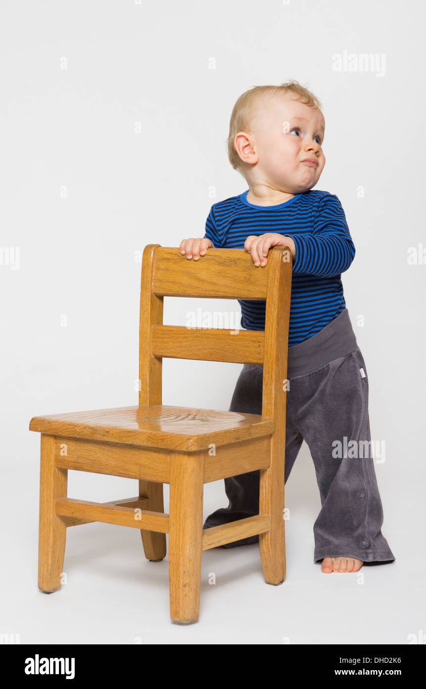 Baby boy with sad face holding onto chair, studio shot Stock Photo - Alamy