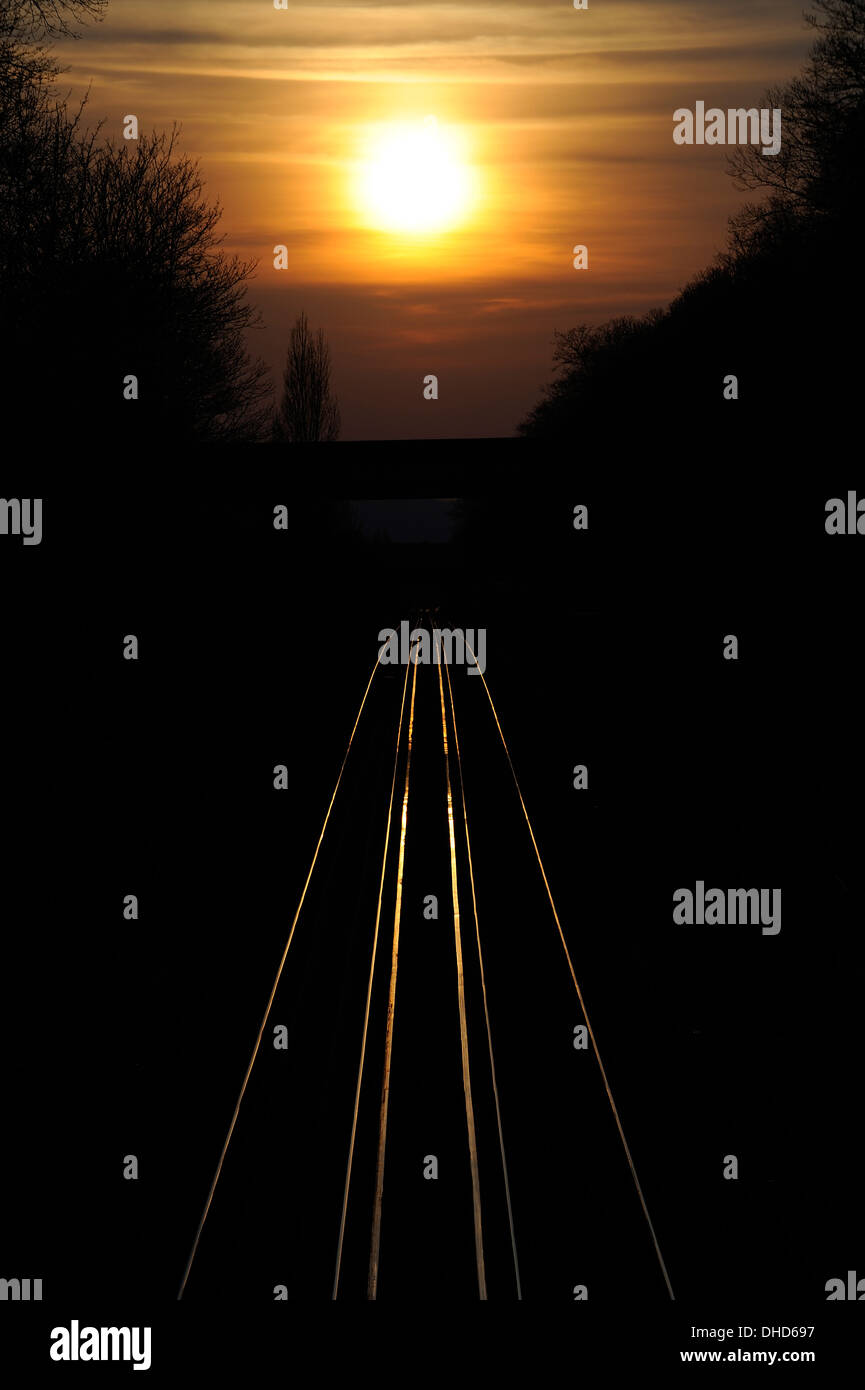 train tracks shining in the sun light going under a bride towards the ...