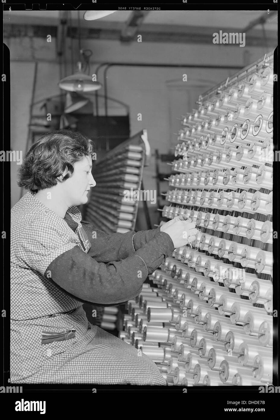 A textile worker in Paterson, New Jersey, shown operating a creel with ...