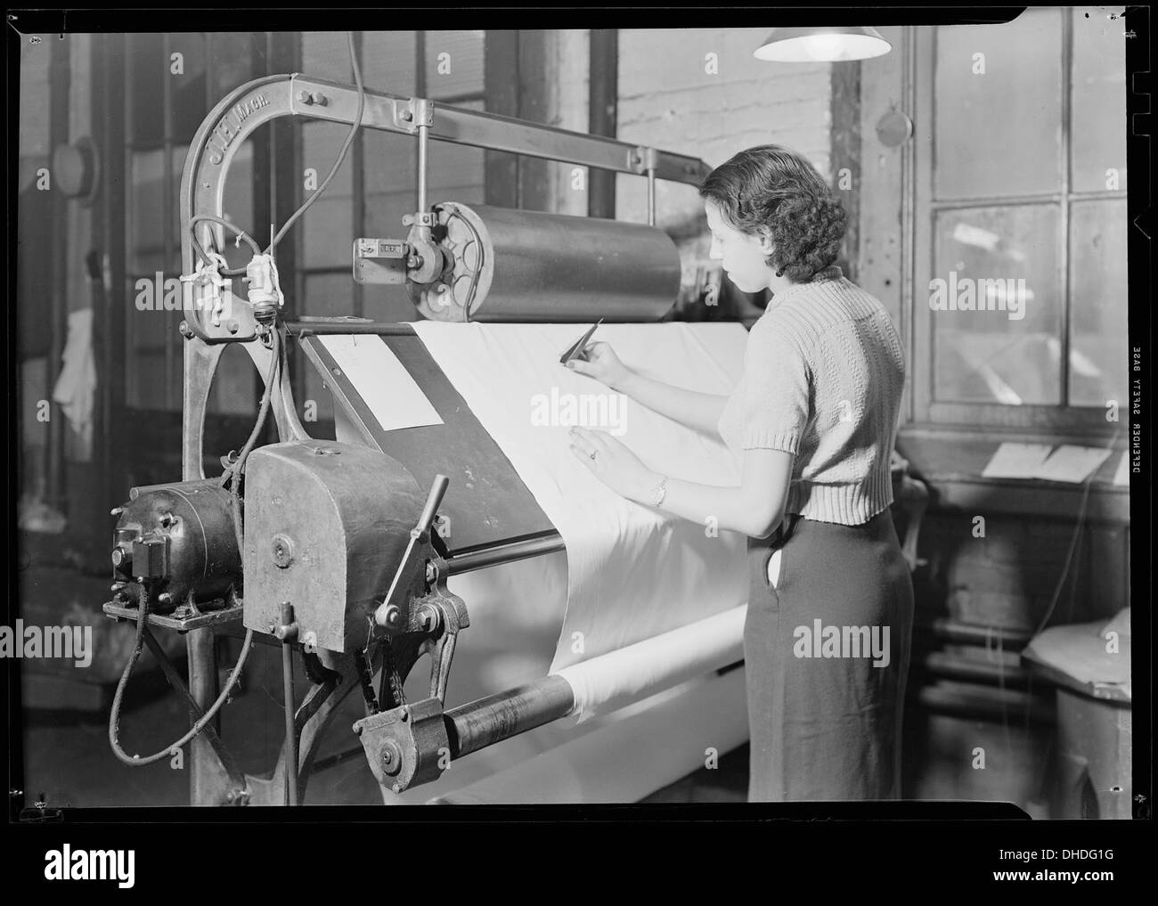 This photograph shows workers examining and picking fabric in a textile ...
