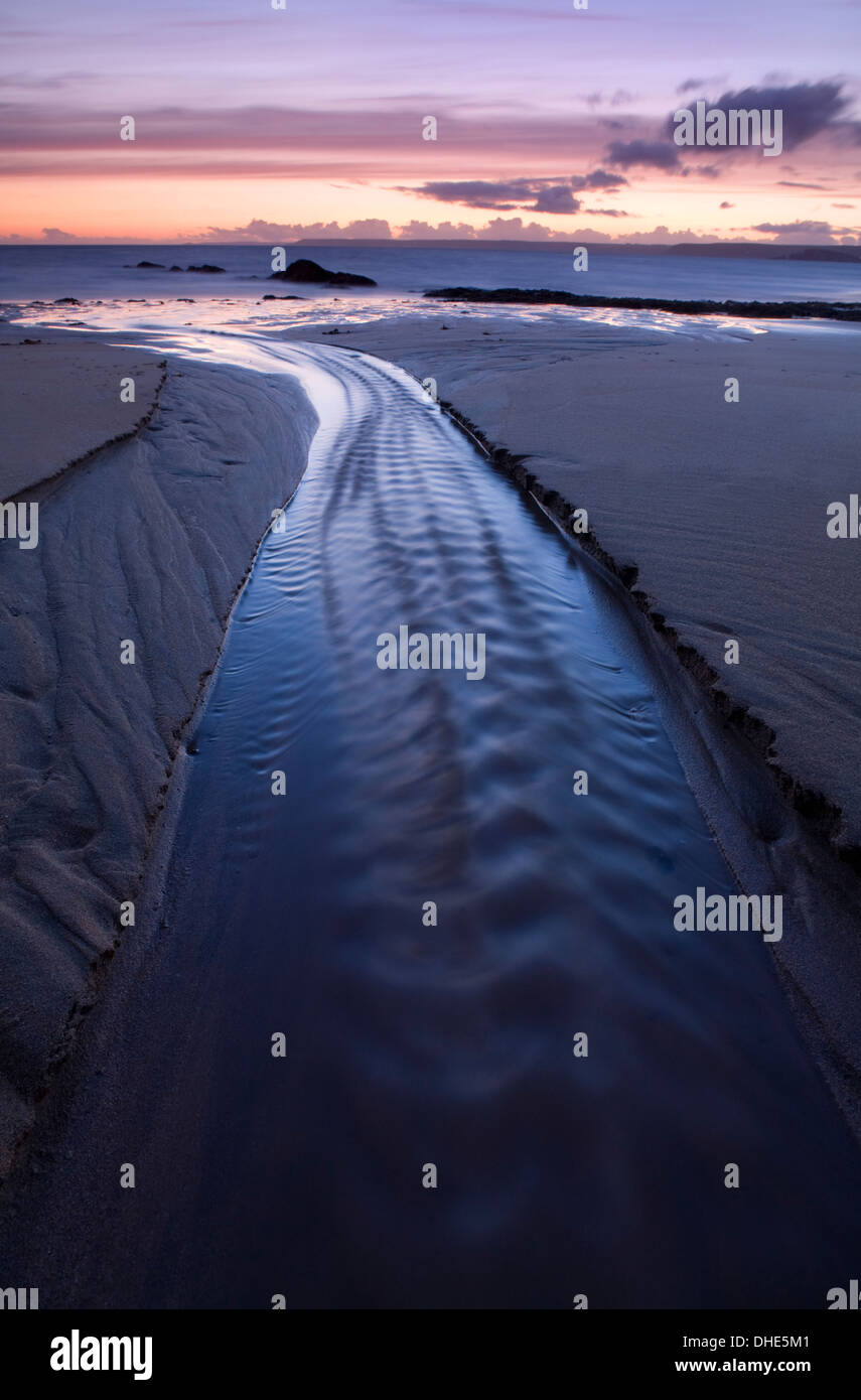 A stream cuts a path through the sand into the sea at Hope Cove, Devon ...