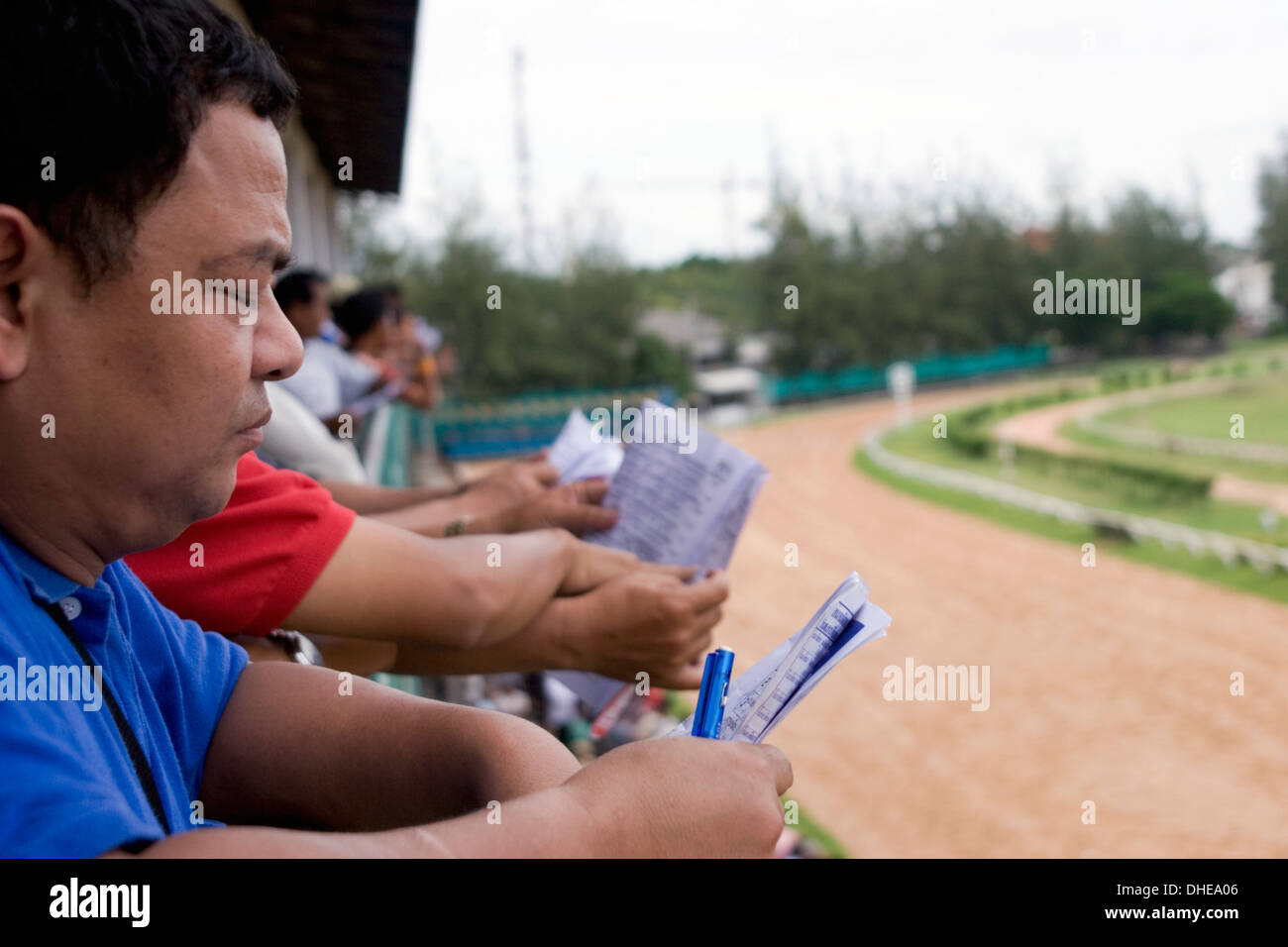 Horse racing fans are lined up at the railing watching throughbred ...