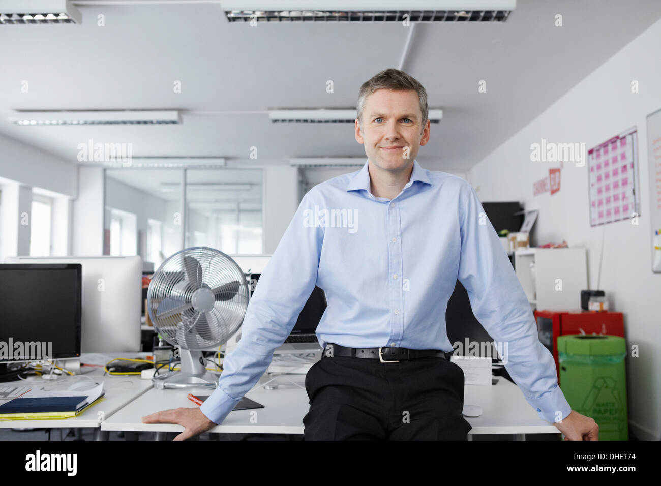 Men sitting on desk in office Stock Photo - Alamy