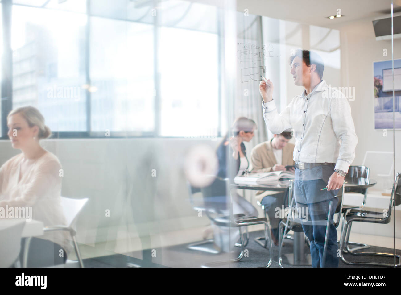 Man writing on glass wall, colleagues in background Stock Photo - Alamy