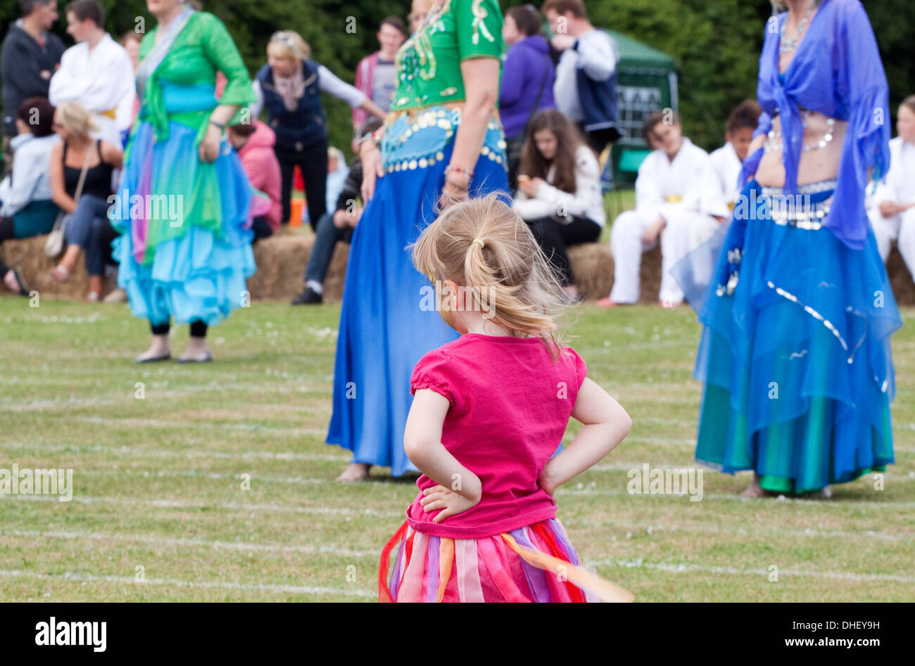 Small girl with hands on hips looks at a group of dancers at an outdoor ...