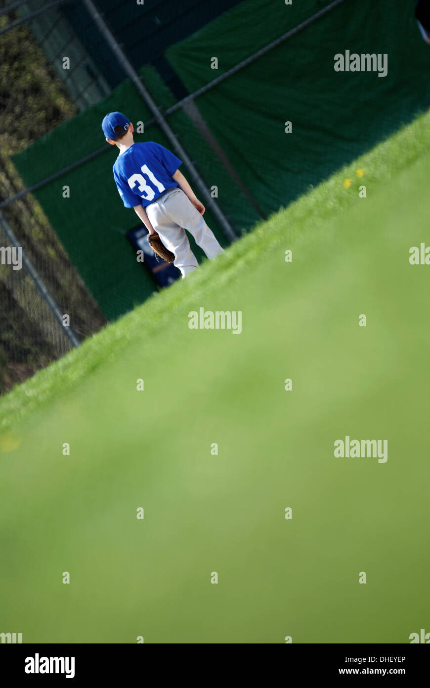 A boy in a blue uniform stands alone in the outfield during a baseball ...