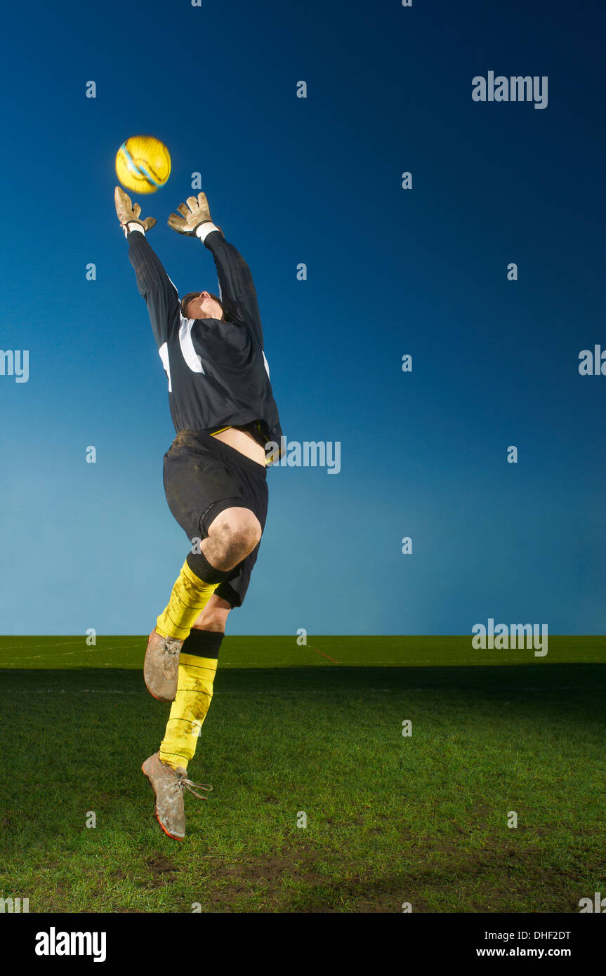 Goalkeeper jumping to catch football Stock Photo - Alamy