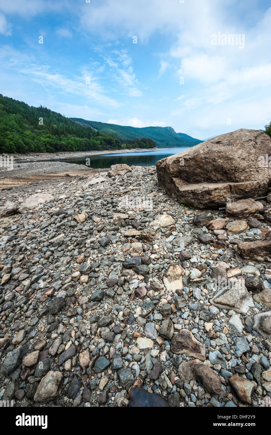 Pebbles and rocks on lakeside beach with hills and woodland beyond ...