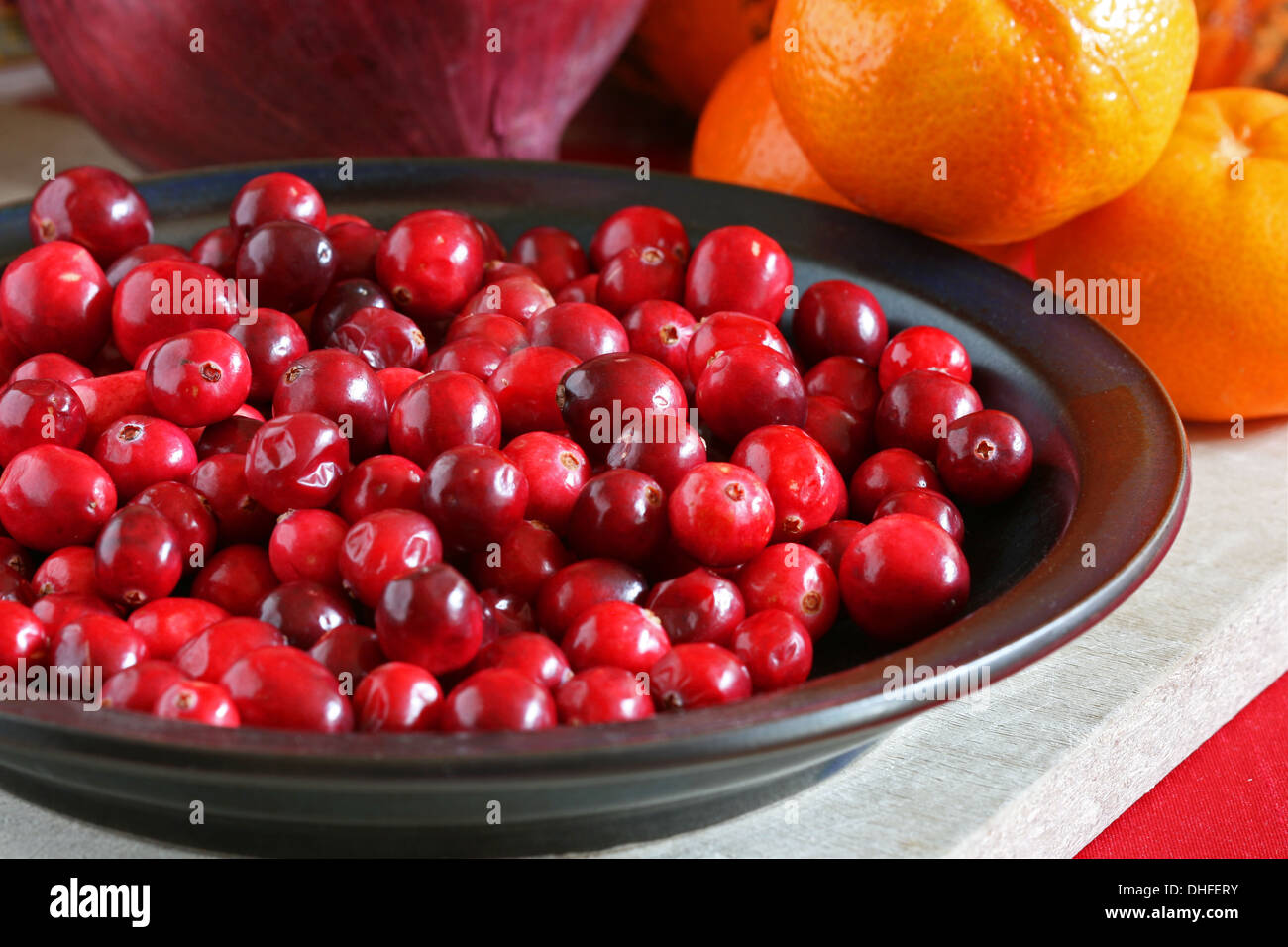 Closeup of bright red cranberries on a dark plate, with clementines and ...
