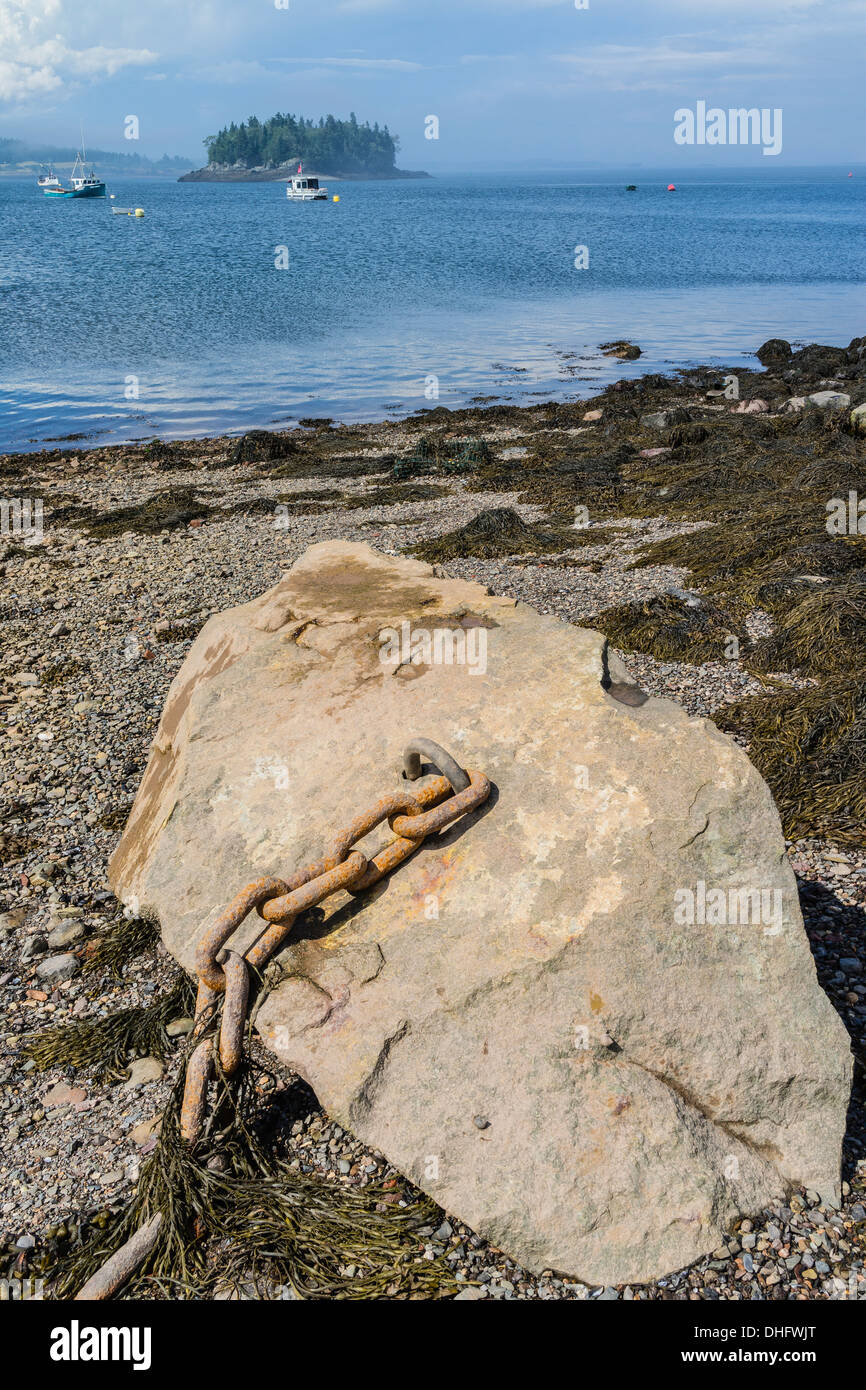 An anchor chain attached to a large boulder lies on a on rocky shore in ...