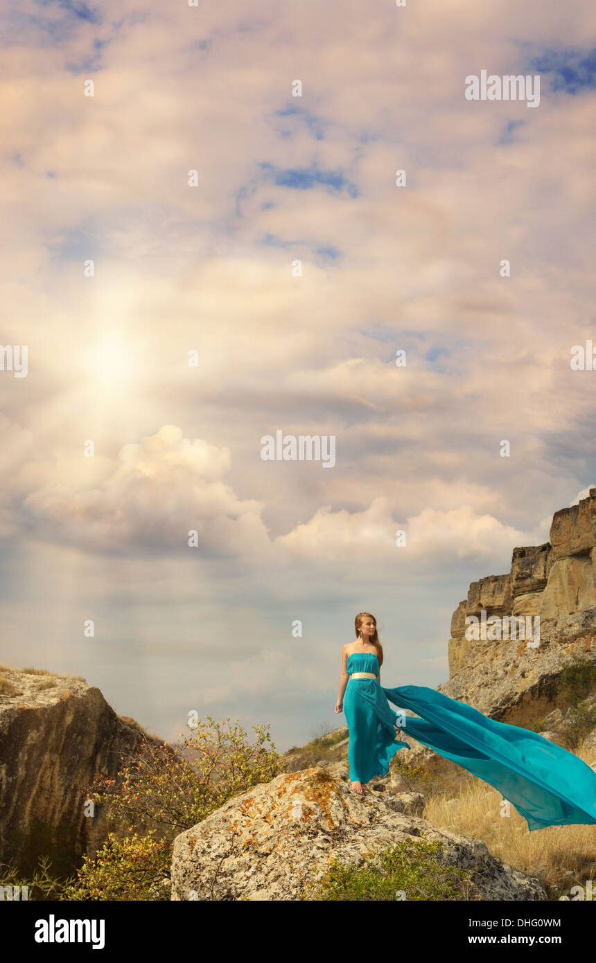 Young beautiful alone woman in dark cyan dress stands on the rock with ...