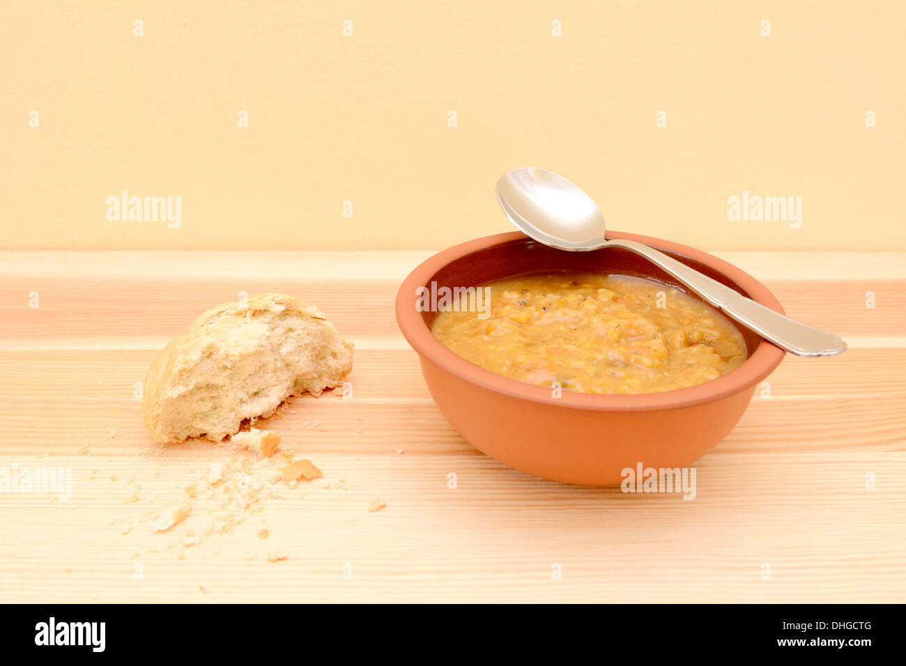 Spoon resting on a bowl of soup, with half a crusty bread roll and ...