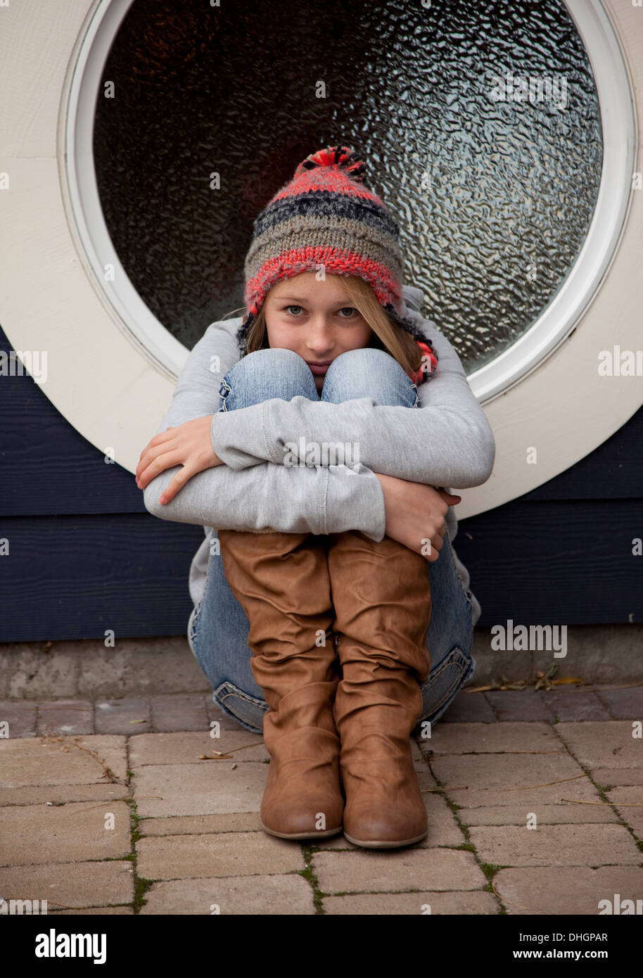 Outdoor photo of young teenage girl seated on ground, hugging knees ...