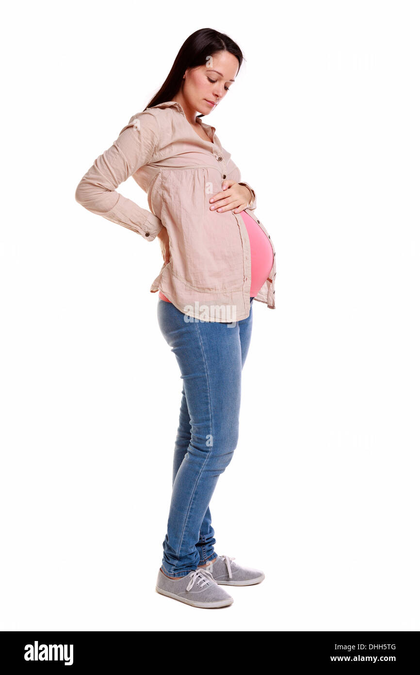 A pregnant woman with her hands on her back looking down at her bump ...